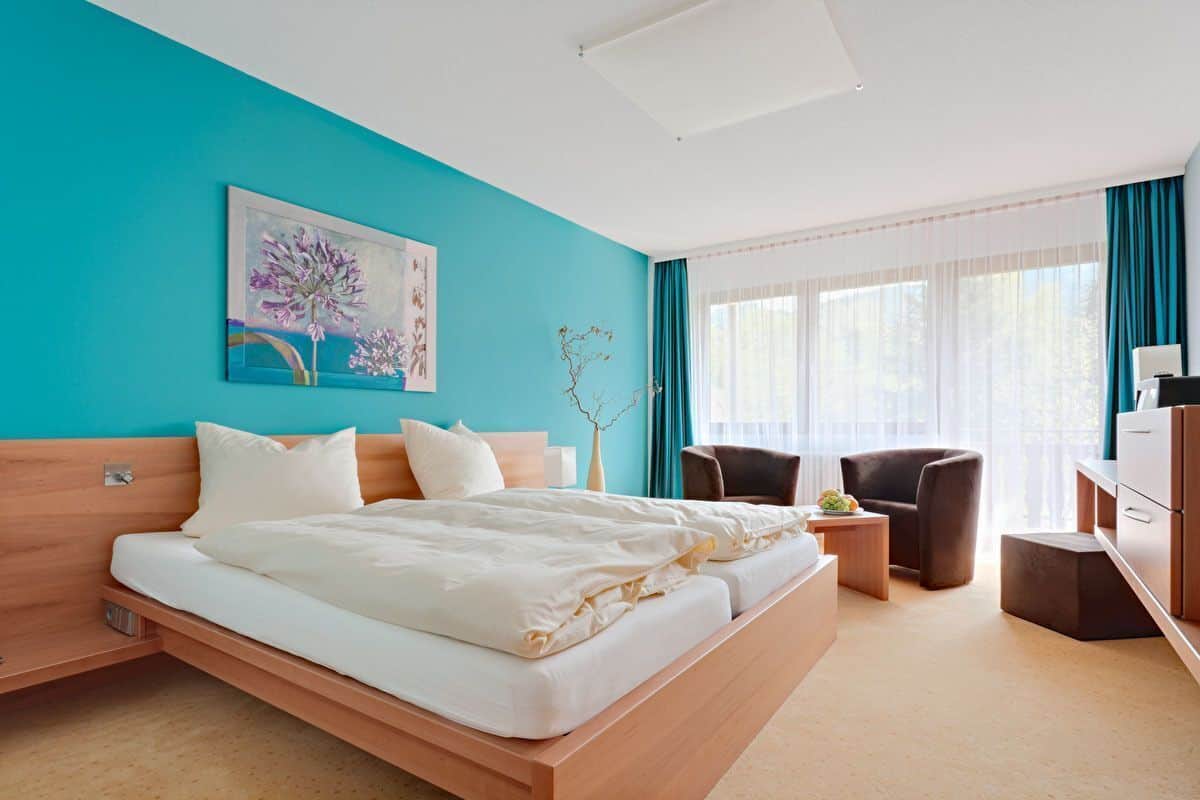 Quarto de hotel com uma cama, uma cadeira, uma escrivaninha e um quadro na parede.