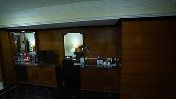Quarto de hotel com parede de painel de madeira, um espelho grande, uma escrivaninha com telefone e uma cadeira.