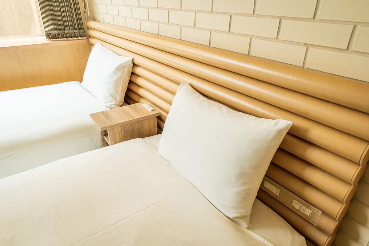 Quarto de hotel com duas camas, um painel de cabeceira de madeira e uma pequena mesa de cabeceira de madeira.