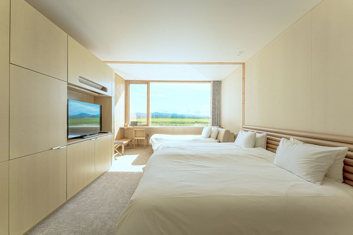 Quarto de hotel moderno com duas camas, uma televisão e uma secretária com uma cadeira.