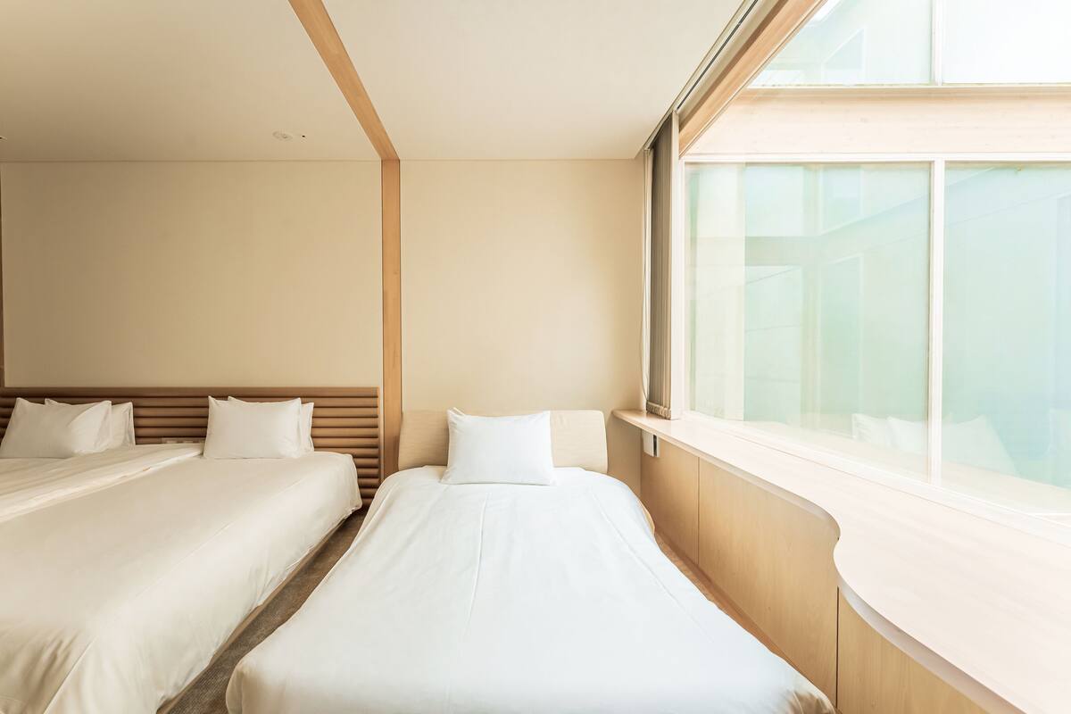 Quarto de hotel com duas camas, uma janela grande e cabeceira de madeira.