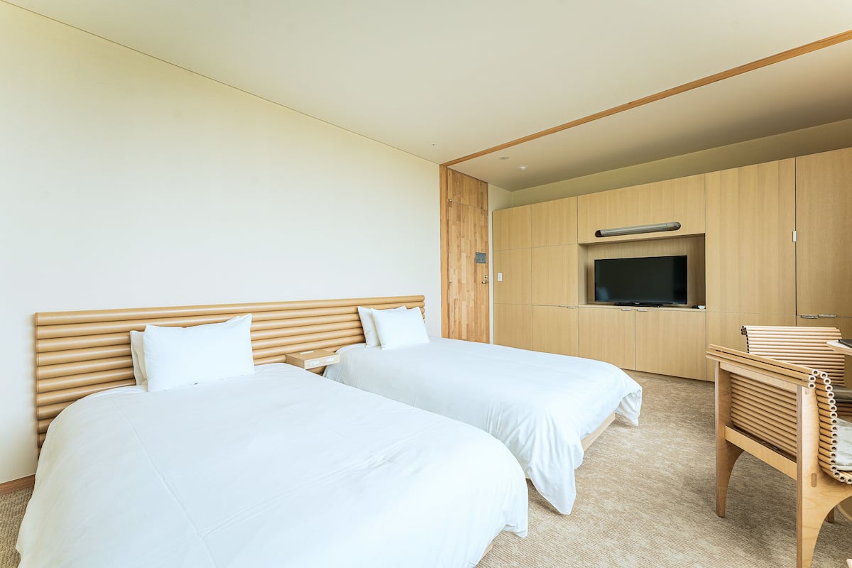 Quarto de hotel com duas camas, televisão e mobiliário de madeira.