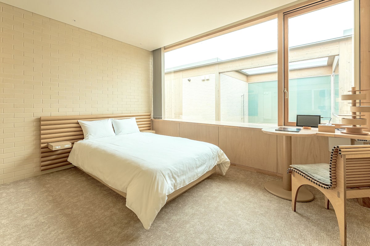 Quarto com cama, escrivaninha com computador e janela com vista para o exterior.