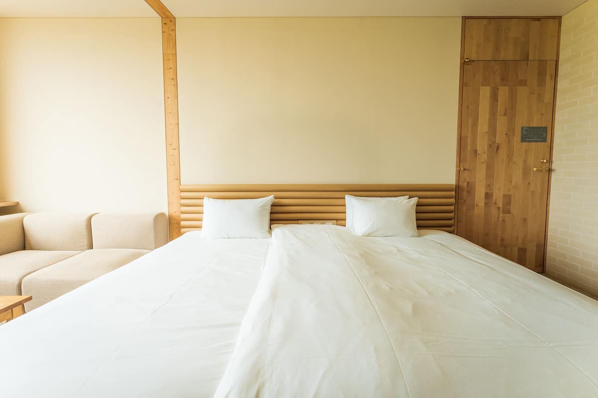 Quarto com cama grande, cabeceira de madeira, guarda-roupa de madeira e sofá bege.