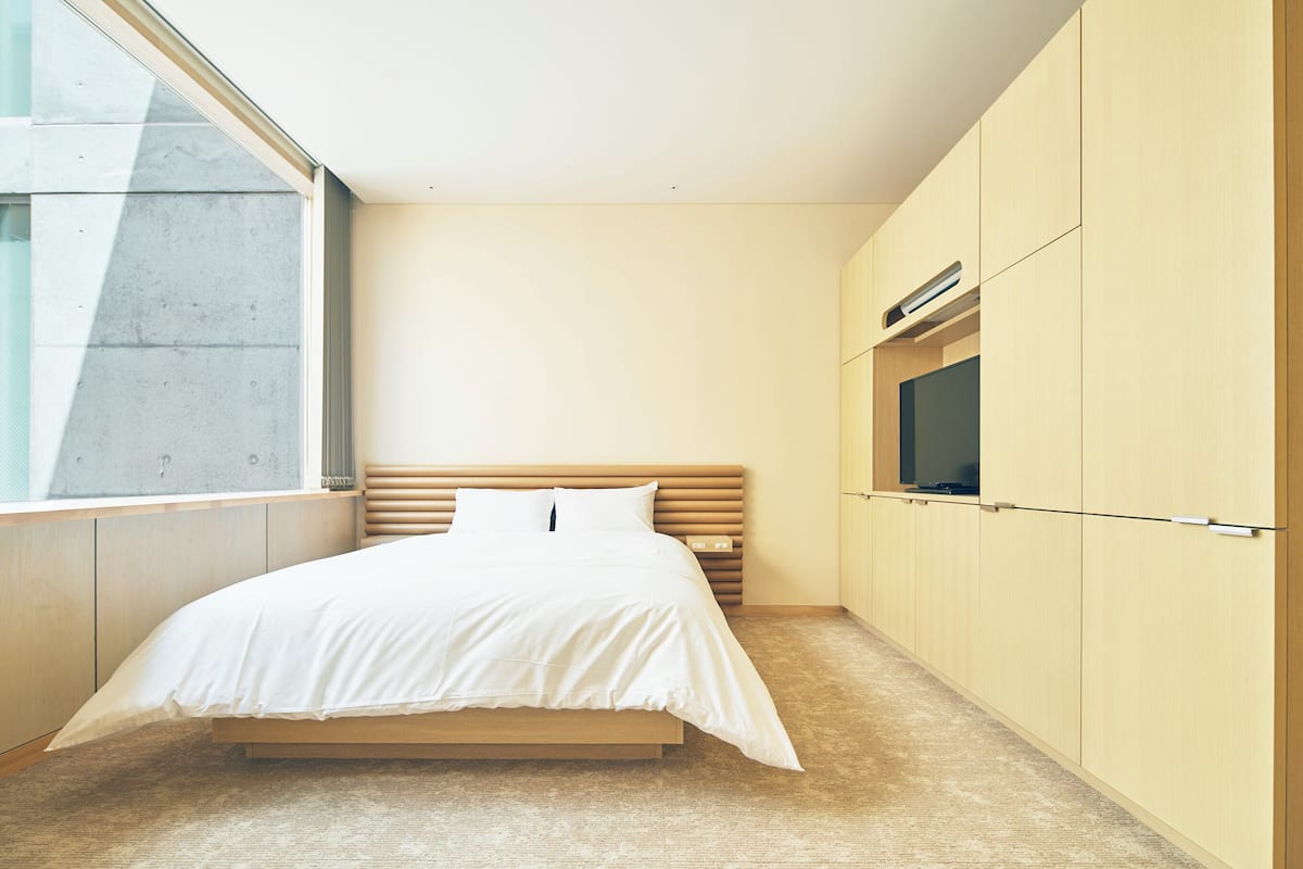 Quarto moderno com cama, TV integrada e amplas janelas.