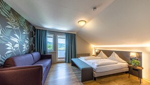 Quarto de hotel moderno com cama, sofá, um banquinho e vista para o exterior.