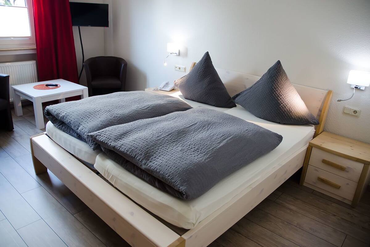 Quarto bem arrumado com cama, mesas de cabeceira, poltrona, televisão e escrivaninha.
