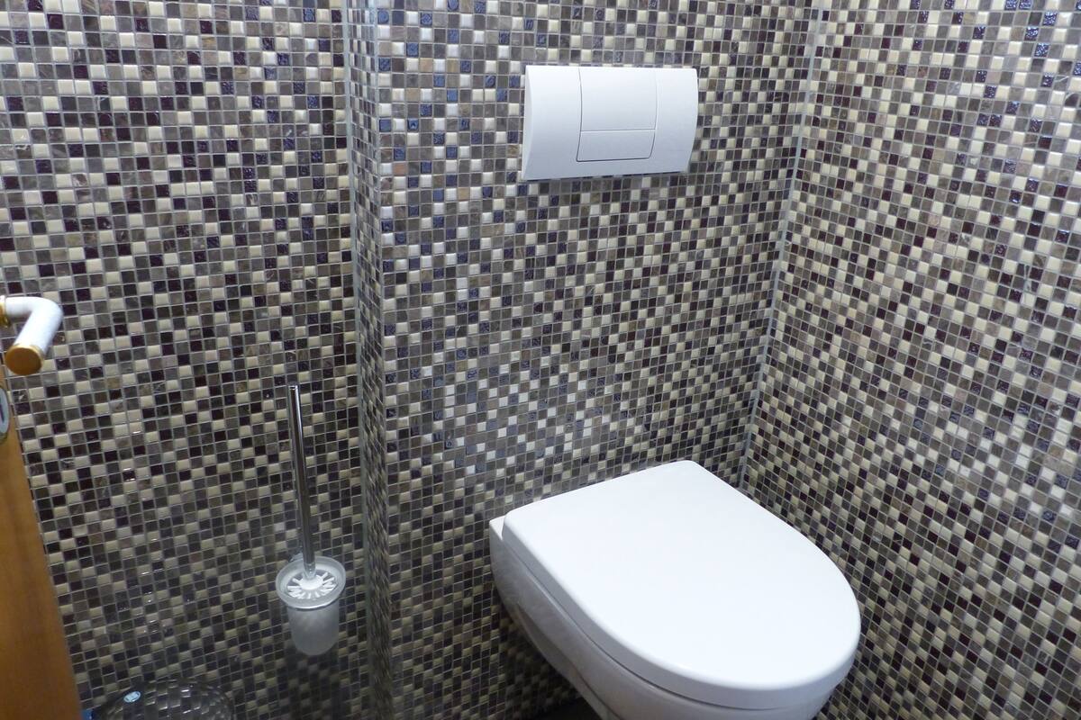 Casa de banho com parede em mosaico de azulejos, sanita branca e cabine de duche em vidro.