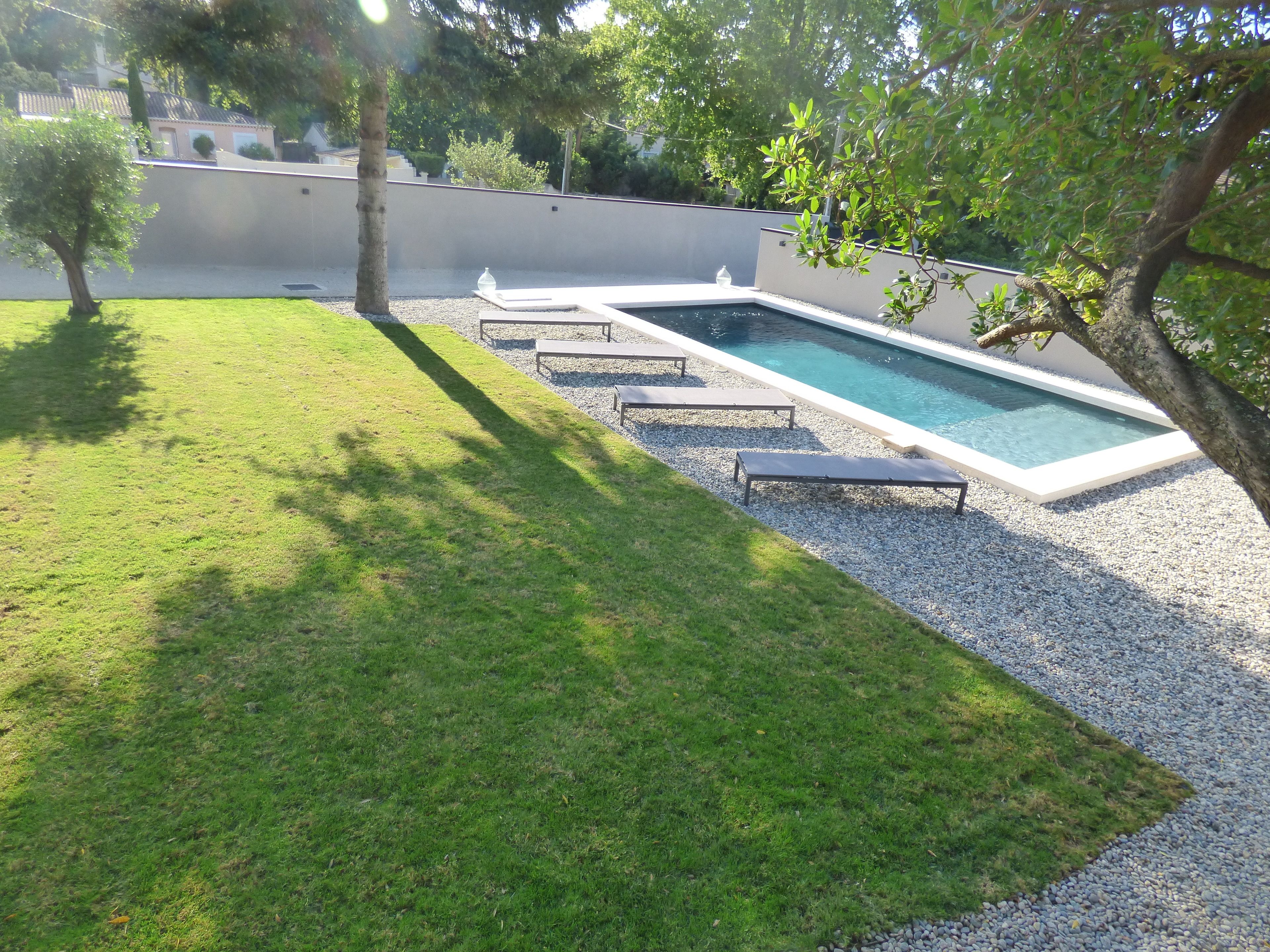 Uma piscina retangular com borda branca, rodeada por uma área de cascalho e quatro espreguiçadeiras.