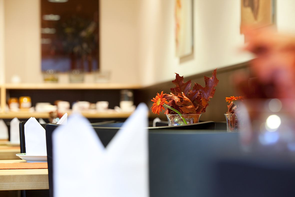 Interior de restaurante com mesas, cadeiras e um vaso com flores laranjas.