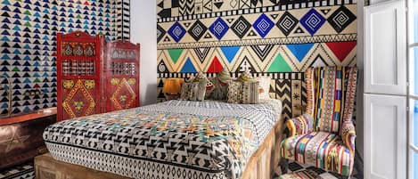 Um quarto com colcha estampada, um armário vermelho e uma parede com desenhos geométricos.