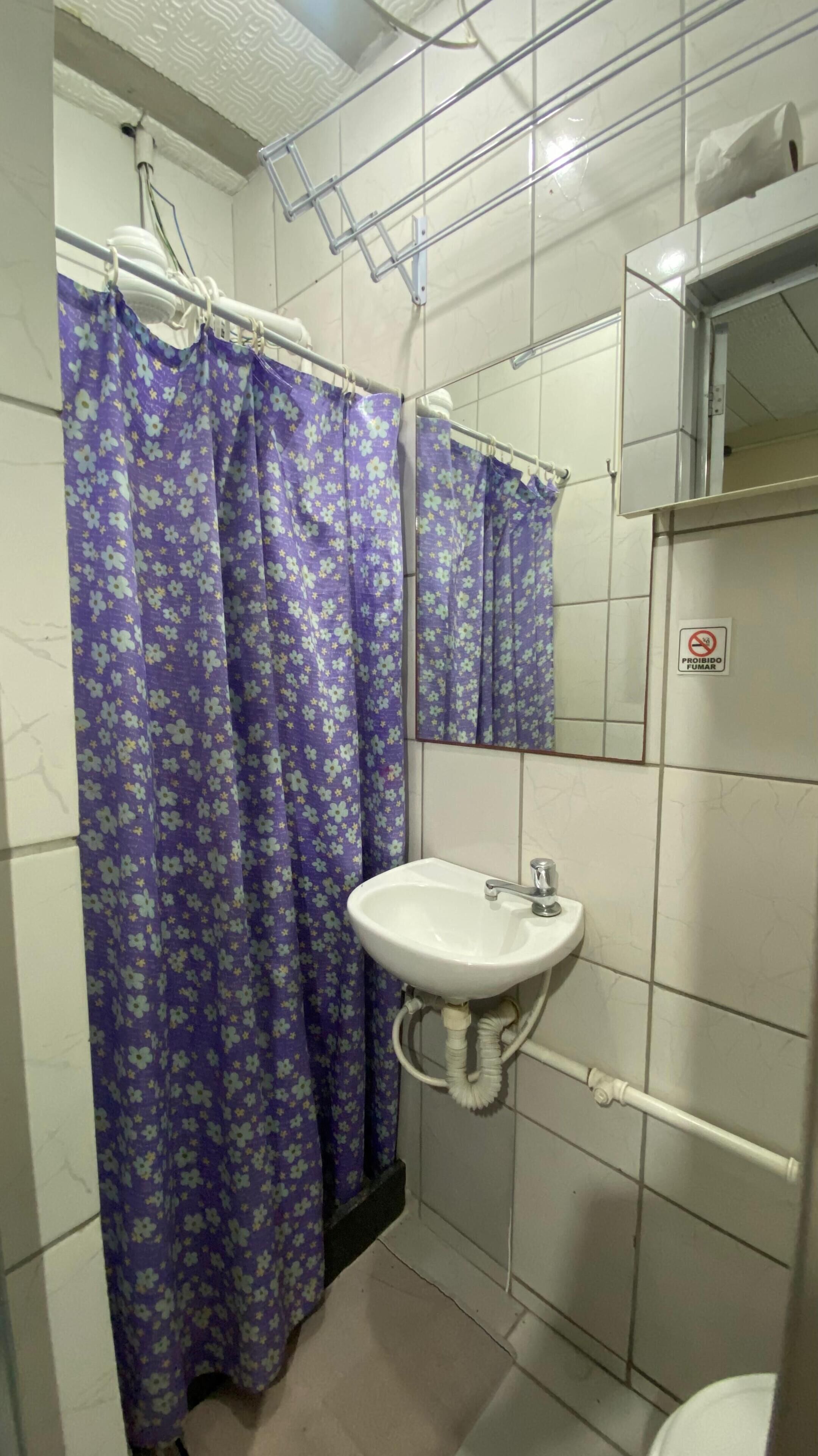 Uma casa de banho com uma pia branca, uma cortina de chuveiro com padrão floral e um sinal de proibido fumar na parede.