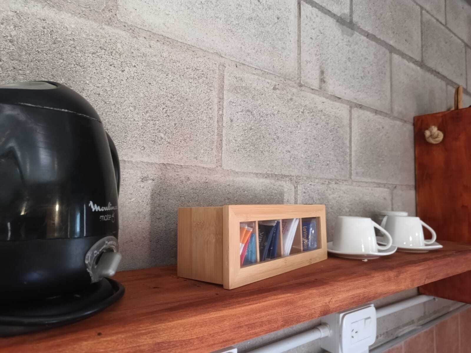 Uma bancada de cozinha com uma cafeteira, um porta-retrato de madeira e xícaras brancas.