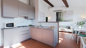 Uma cozinha moderna com micro-ondas embutido, fogão e pia, uma área de jantar com mesa e cadeiras, e uma sala de estar com sofá e um quadro.
