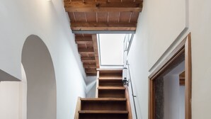Uma escada de madeira com soalho em azulejos, que dá acesso a um quarto com porta e luminária.