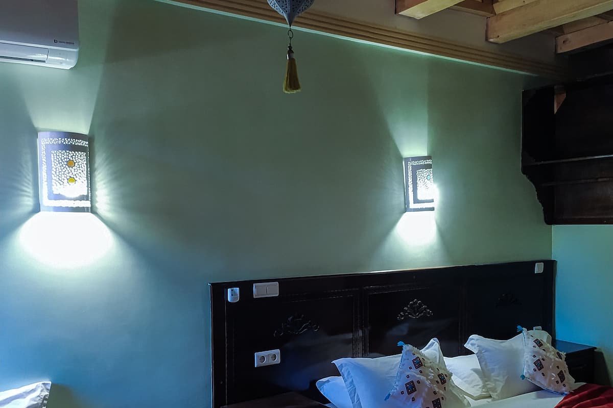Quarto com teto de madeira, cama com roupa de cama branca e vermelha, duas mesas de cabeceira e um banquinho vermelho.