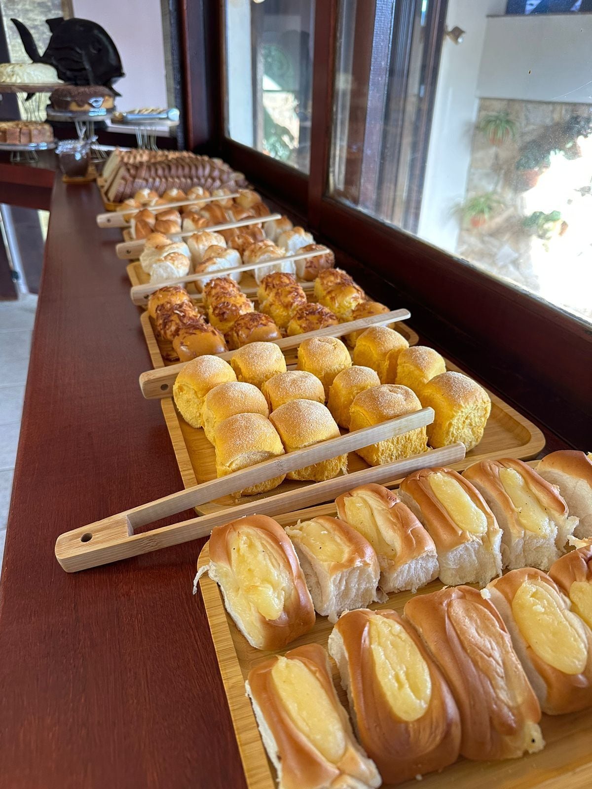 Um buffet com diversos produtos de panificação, incluindo pães e doces, expostos em tábuas de madeira.