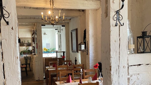 Uma área de jantar rústica, com mesas e cadeiras de madeira, um candelabro e uma parede de tijolos.