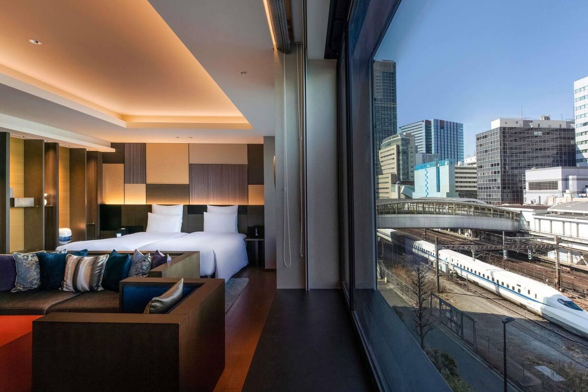 Quarto de hotel moderno com uma cama grande, área de estar e vista para a cidade.