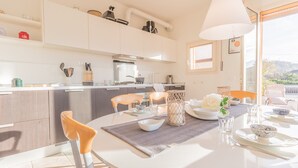 Cozinha moderna com armários brancos, área de jantar com mesa redonda e vista para o exterior.