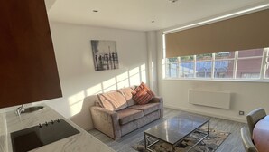 Uma sala de estar moderna com sofá, mesa de centro e área de cozinha com bancada e pia.
