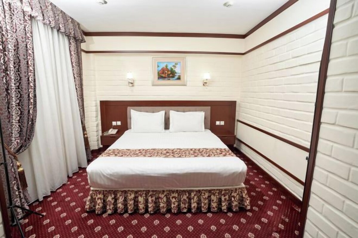 Quarto de hotel com uma cama grande, cabeceira, pintura na parede e tapete estampado.
