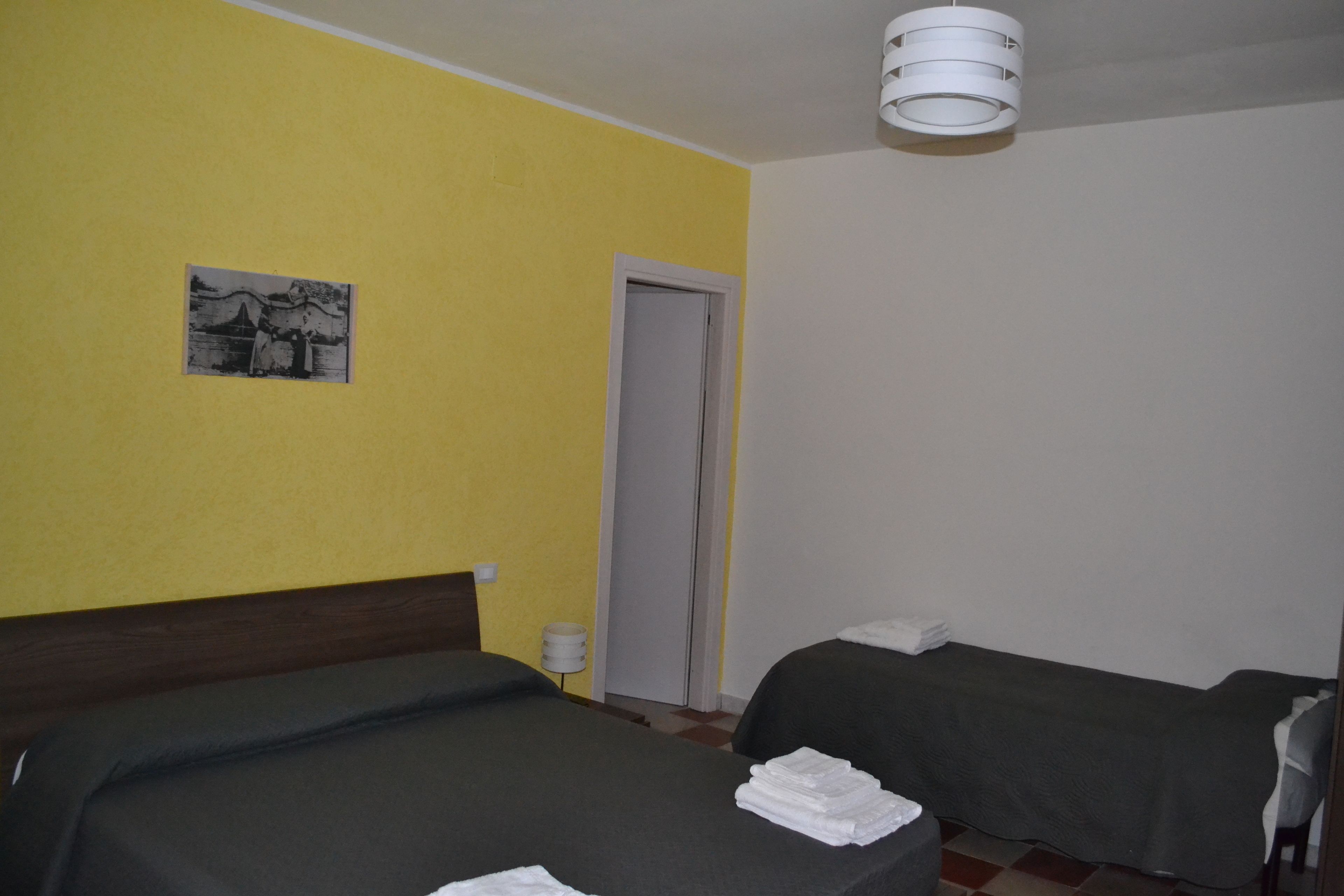 Quarto de hotel com duas camas, uma porta, um lustre e um quadro pendurado na parede.