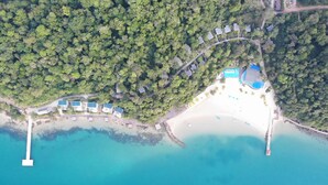 Vista aérea de um resort à beira-mar, com praia, um píer e vários edifícios com piscina.