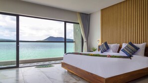 Quarto com cama grande, vista para o mar e parede de painéis de madeira.