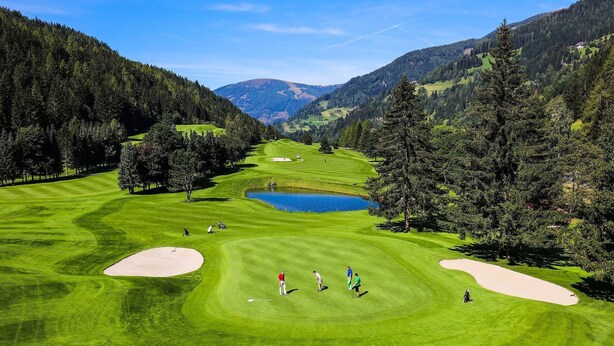 Um campo de golfe com bunkers, um lago e colinas arborizadas.