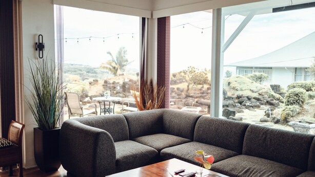 Uma sala de estar moderna com sofá seccional, mesa de centro de madeira e uma grande janela com vista para um jardim e uma casa.