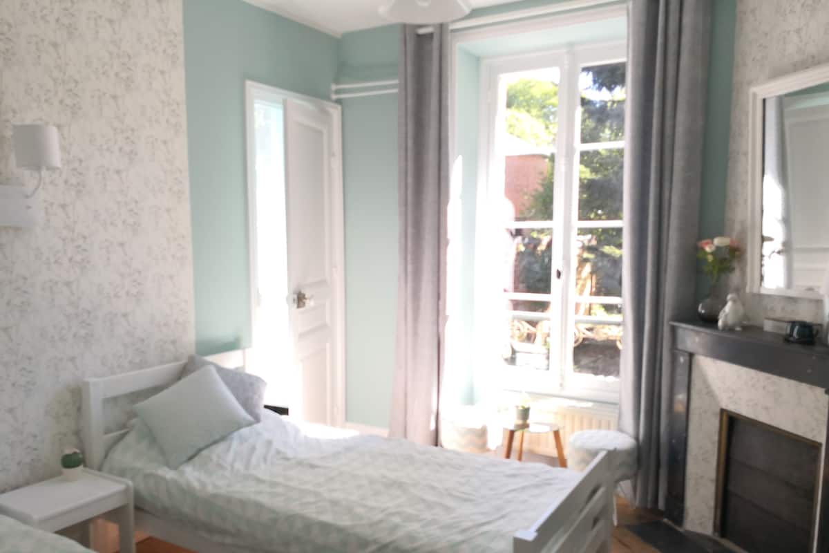 Quarto com cama, mesa de cabeceira, penteadeira, janela com cortinas e lareira.