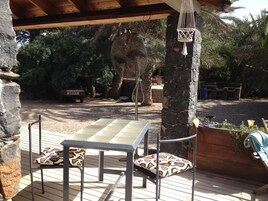 Um pátio externo com mesa e cadeiras, cercado por paredes de pedra e um deck de madeira.