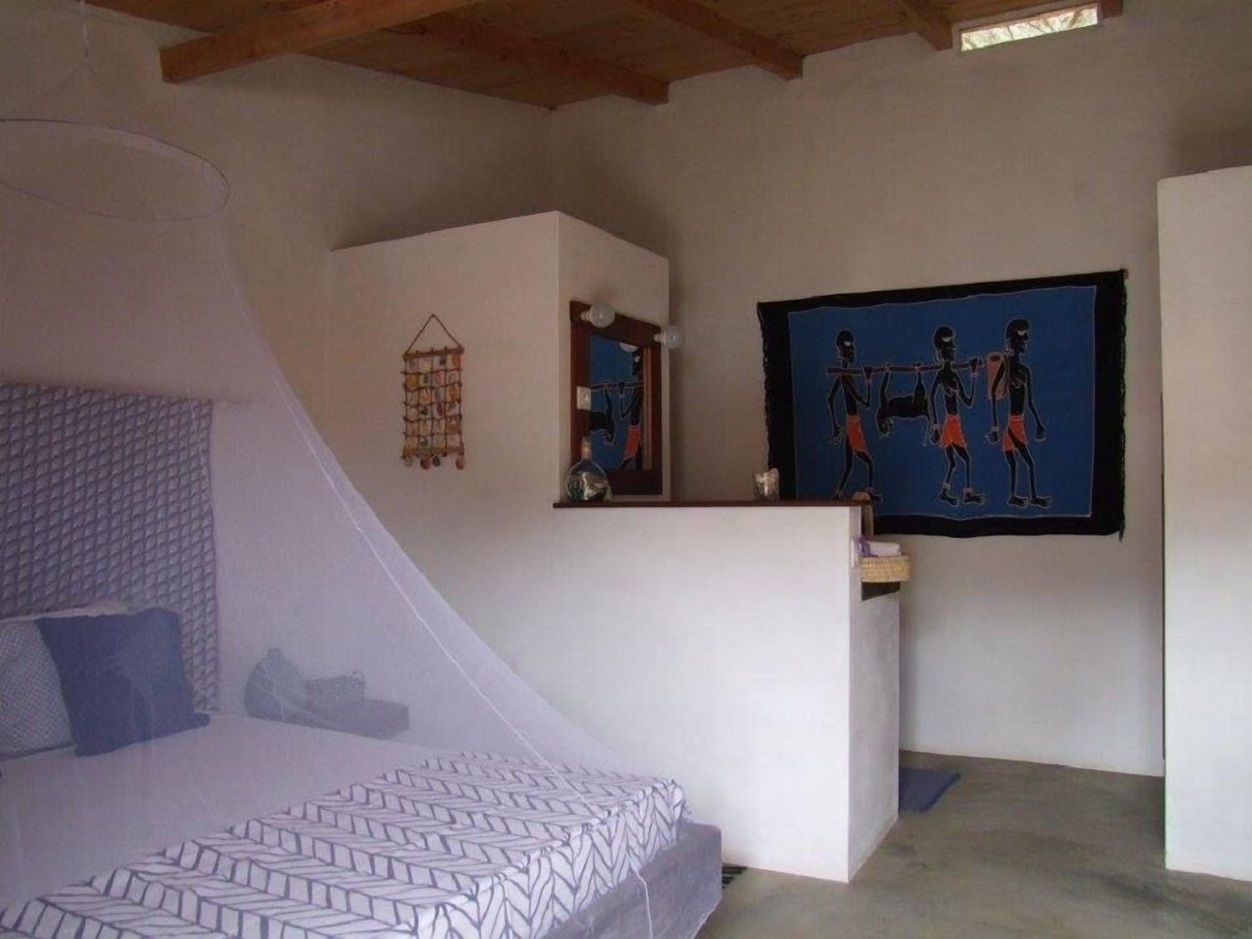 Quarto com cama, mesa de cabeceira, espelho e um quadro na parede.