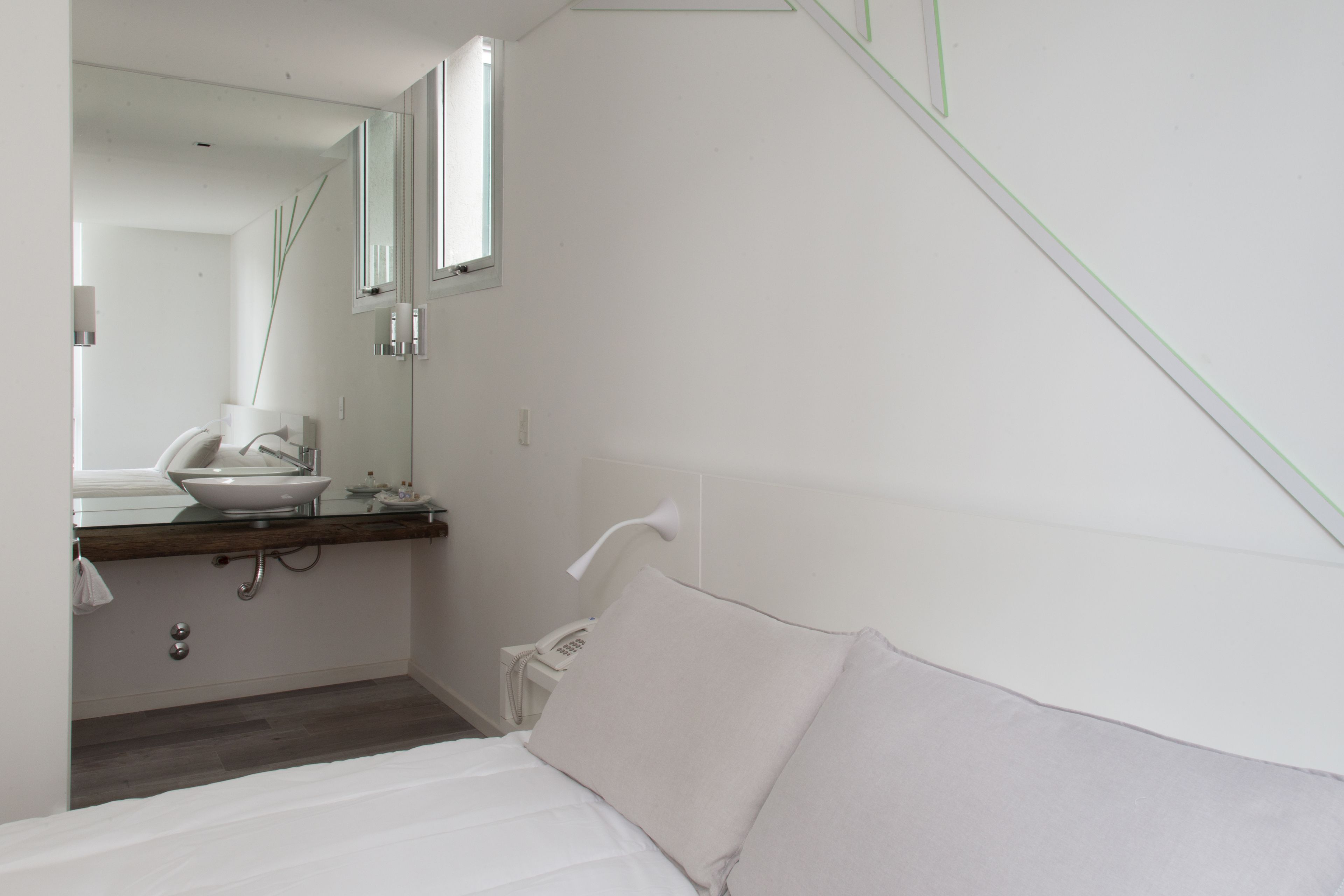 Um quarto com cama, mesa de cabeceira com abajur, espelho e janela.