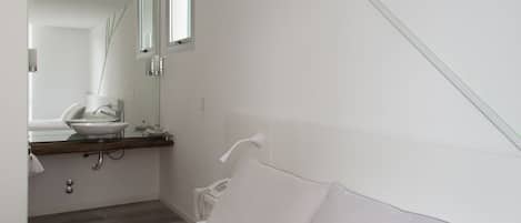 Um quarto com cama, mesa de cabeceira com abajur, espelho e janela.
