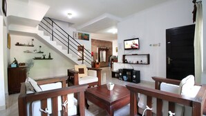 Uma sala de estar com escada, TV fixada na parede e uma porta.