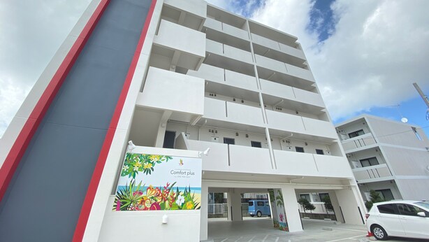Um hotel com vários andares e um letreiro chamativo 'Comfort plus', com varandas e estacionamento com veículos.