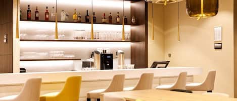 Uma área de bar com um balcão comprido, vários bancos e uma variedade de garrafas e copos nas prateleiras.