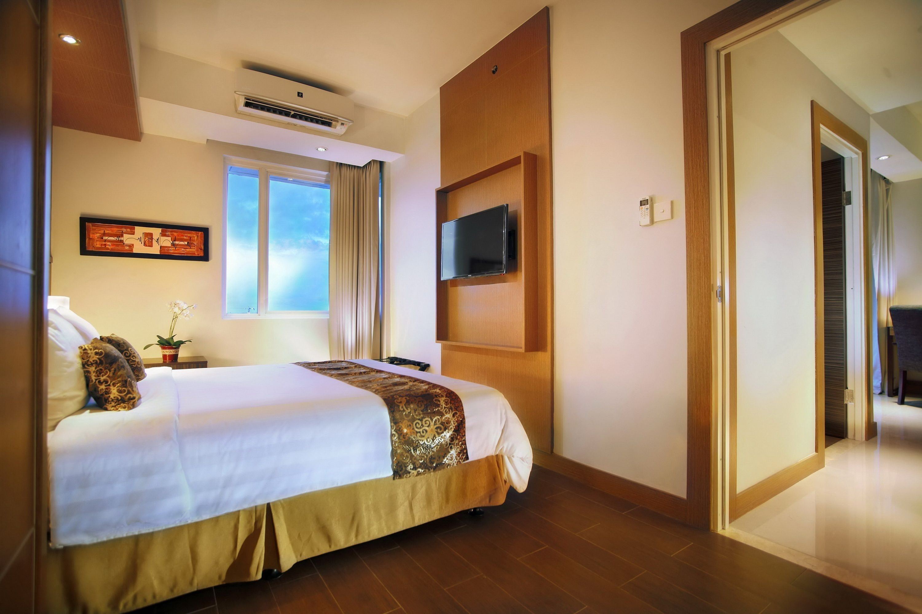 Quarto de hotel com uma cama grande, televisão fixada na parede, janela com cortinas e painel de madeira.