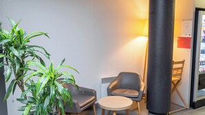 Um lobby moderno com uma planta em vaso, duas poltronas de couro, uma mesa de madeira redonda e um pilar grande.