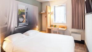 Quarto de hotel com uma cama, uma escrivaninha, uma cadeira, janela com cortinas, televisão e radiador.