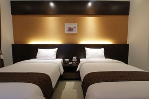 Quarto de hotel com duas camas, uma cabeceira de madeira, mesa de cabeceira com telefone e luminária, e um quadro na parede.