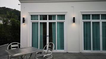 Um edifício moderno com grandes janelas, uma varanda e um espaço de pátio com mesa e cadeiras.