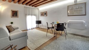 Uma sala de estar moderna com sofá, mesa de jantar com cadeiras, televisão e um quadro pendurado na parede.