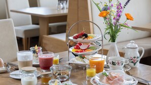 Uma mesa de pequeno-almoço com diversas comidas, bebidas e um vaso de flores.
