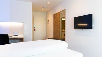 Quarto de hotel com cama, escrivaninha, televisão na parede e painel de madeira.