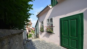Uma rua de paralelepípedos estreita com um edifício branco, com portaria e janelas em verde.