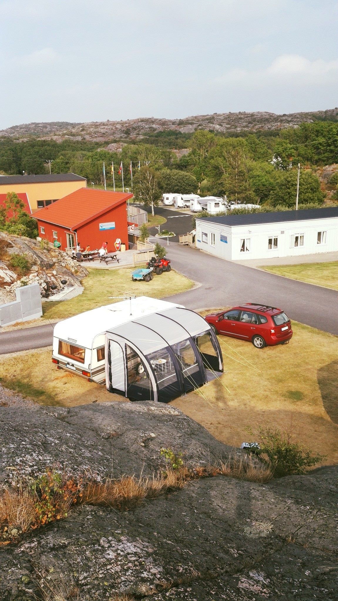 Um camping com uma caravana, um carro vermelho e um edifício com telhado vermelho.