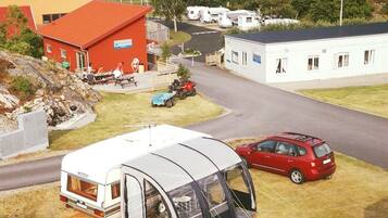 Um camping com uma caravana, um carro vermelho e um edifício com telhado vermelho.